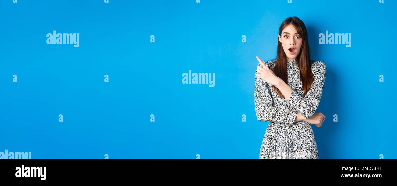 Excited pretty woman in dress pointing at upper left corner, look with ...