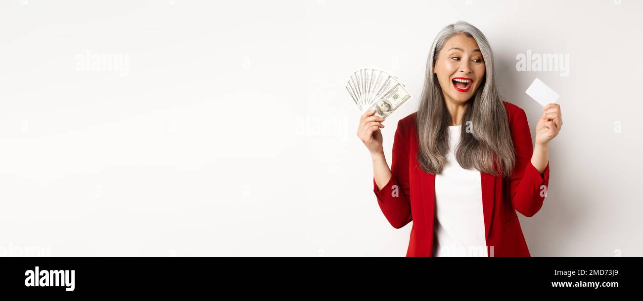 Cheerful asian senior woman earn money, showing dollars in cash and ...