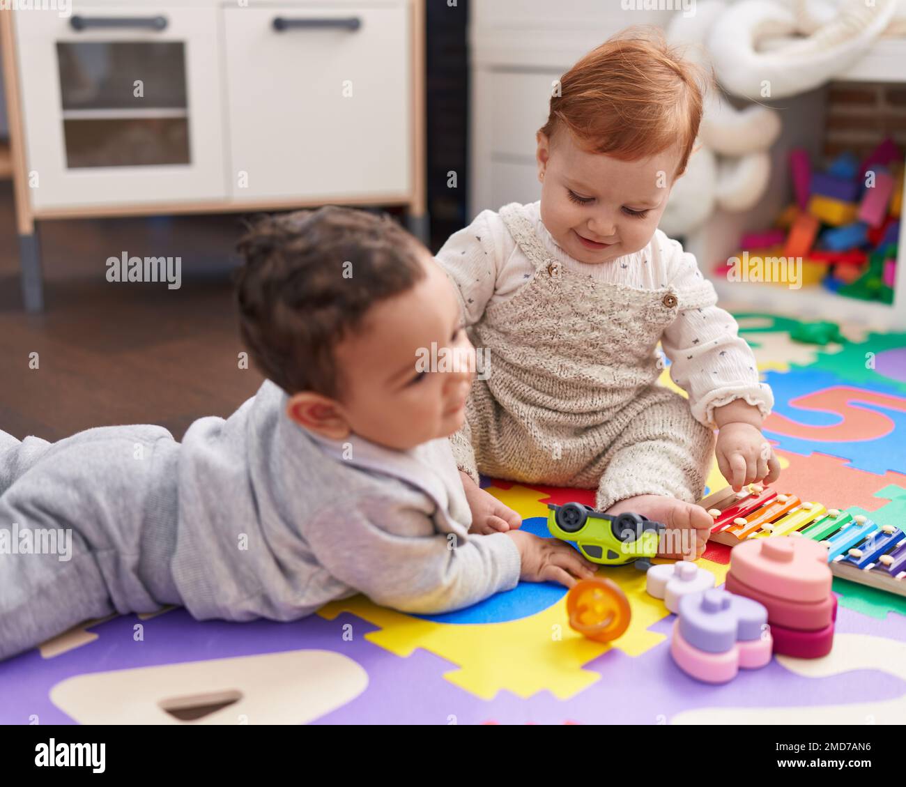 Two adorable babies playing with toys sitting on floor at kindergarten ...