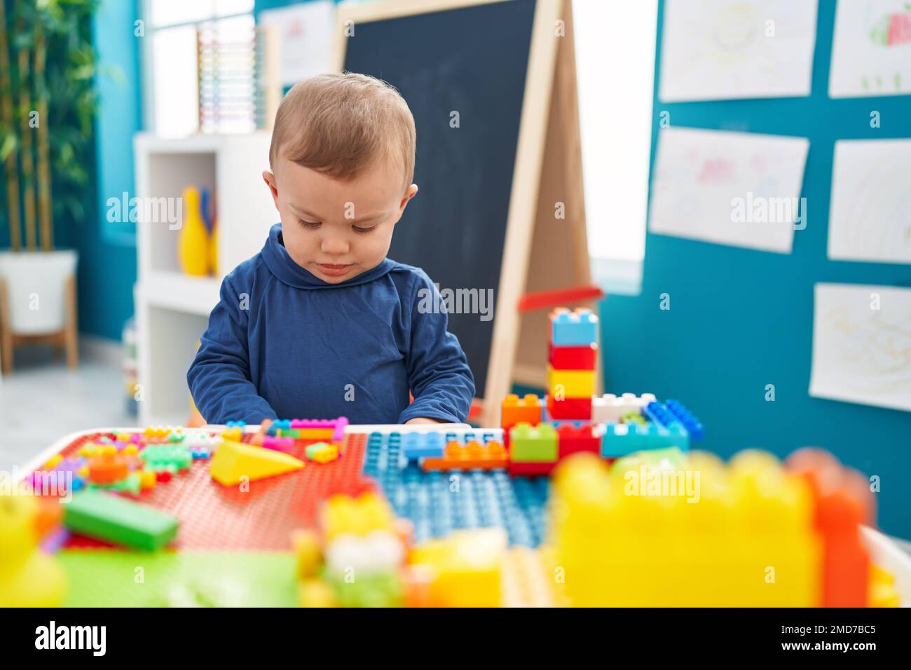 Adorable blond toddler playing with construction blocks standing at ...