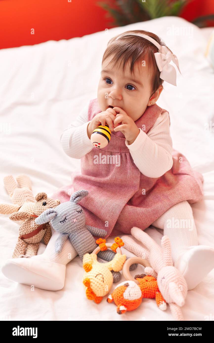 Adorable hispanic baby bitting maraca sitting on bed at bedroom Stock ...