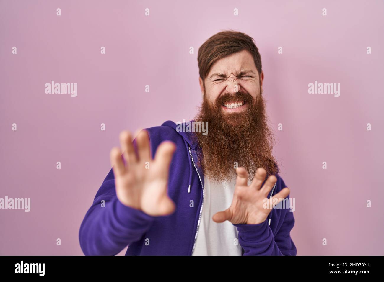 Caucasian man with long beard standing over pink background disgusted ...