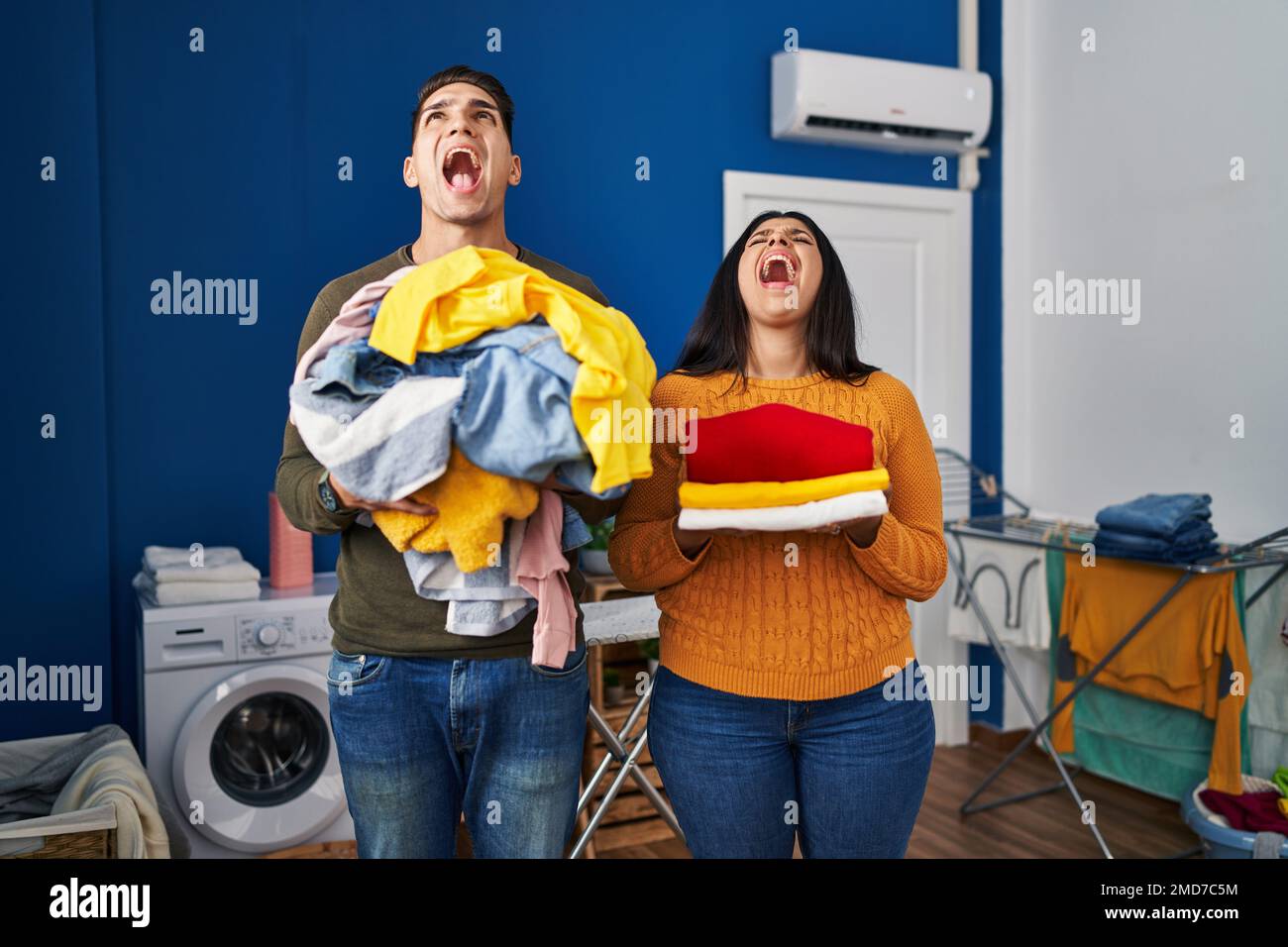 Young couple holding laundry dirty and clean laundry angry and mad ...