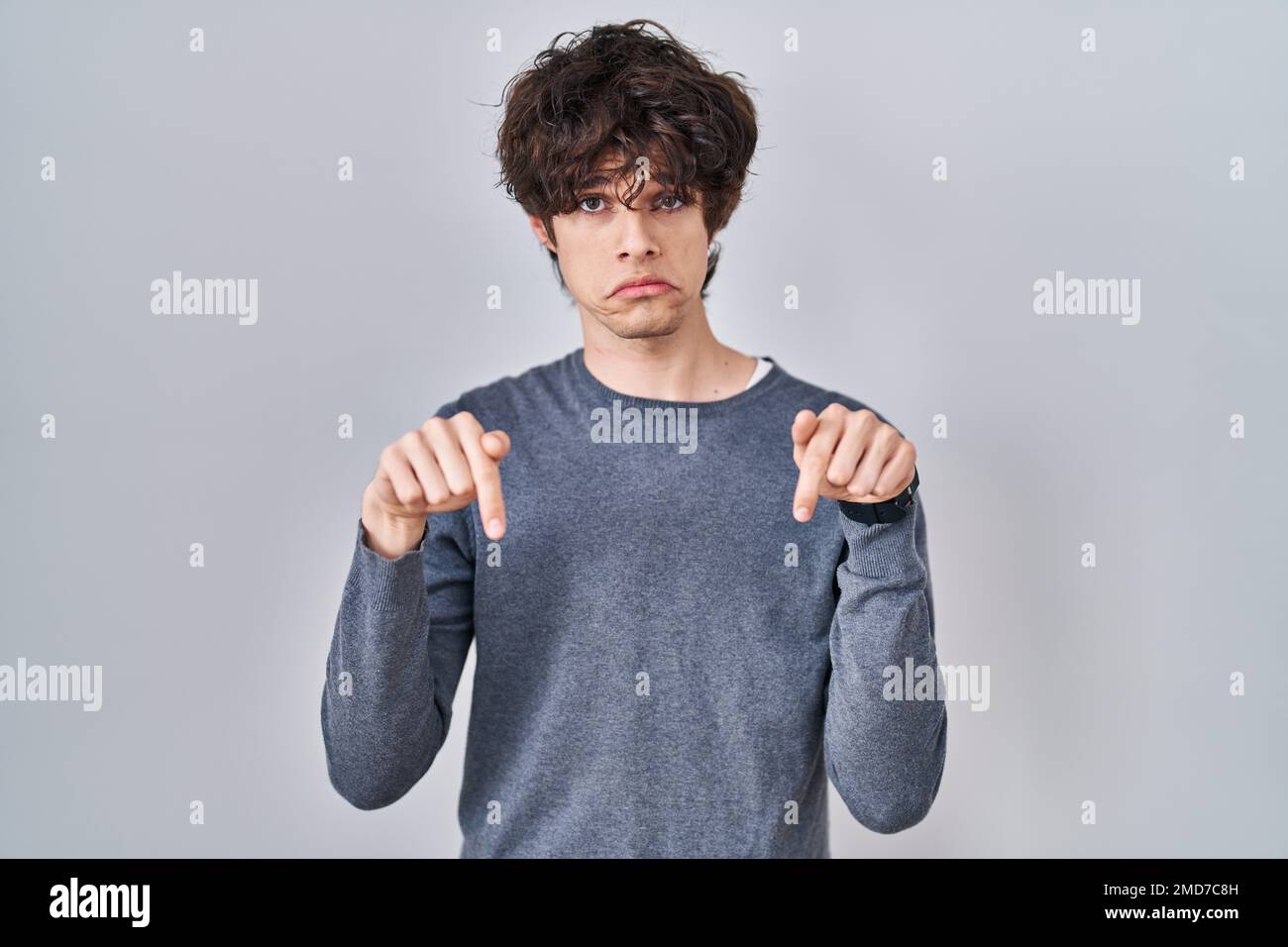 Young man standing over isolated background pointing down looking sad ...