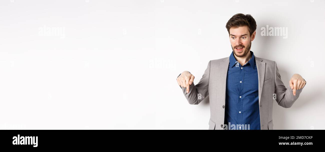 Excited guy in suit smiling and pointing fingers down, looking at ...