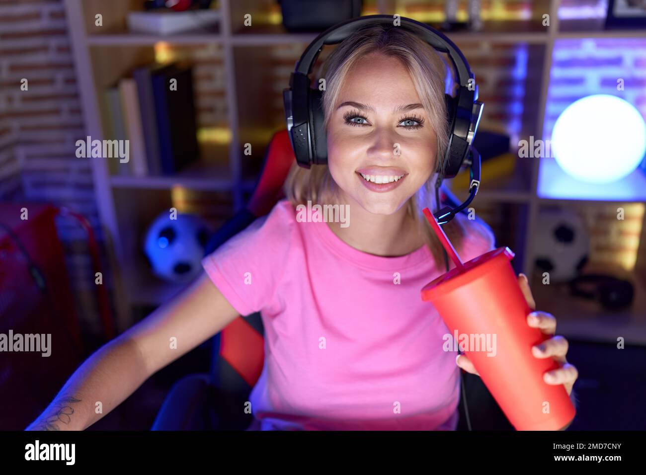 Young blonde woman streamer playing video game drinking beverage at ...