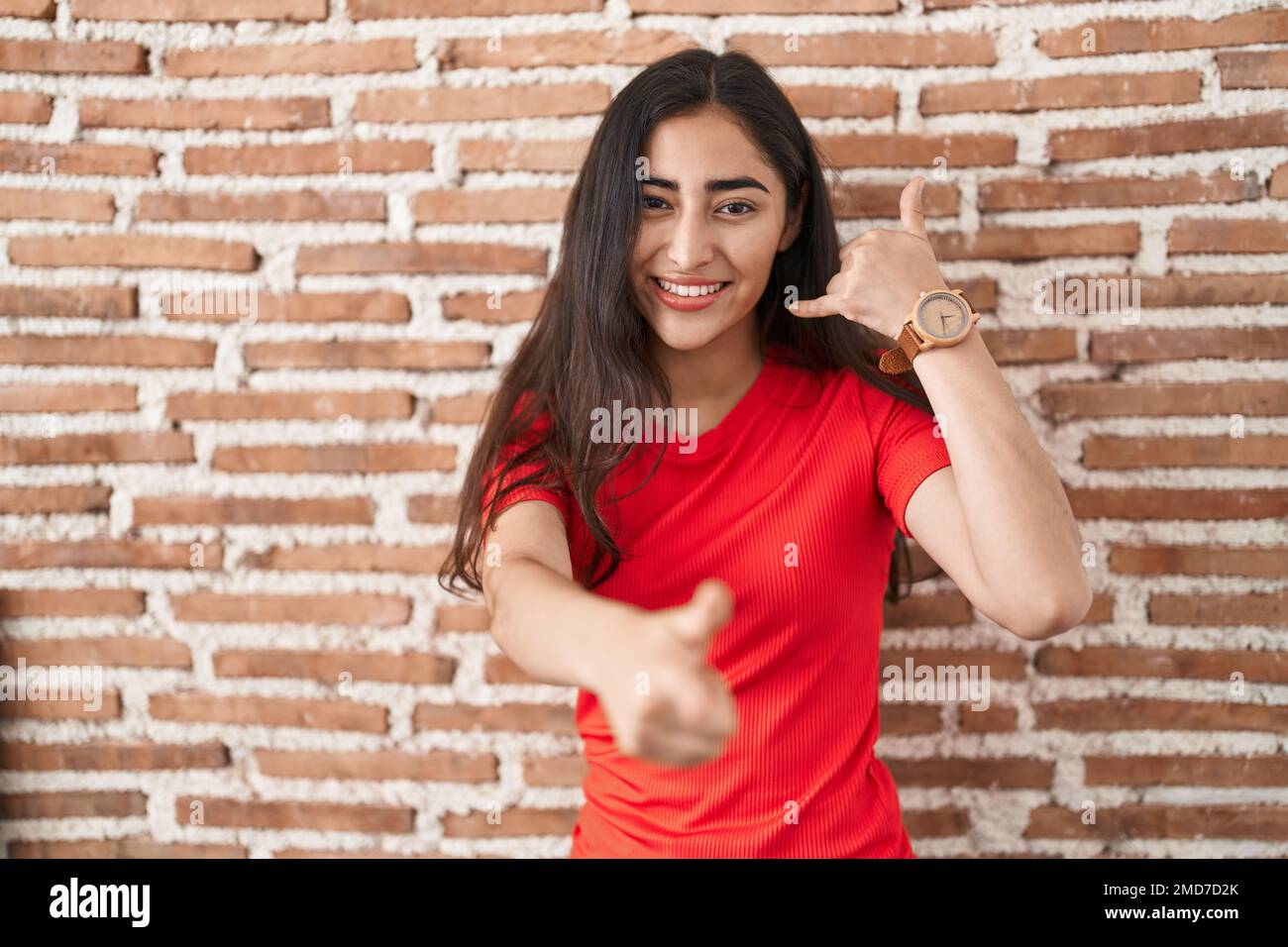 Young teenager girl standing over bricks wall smiling doing talking on ...