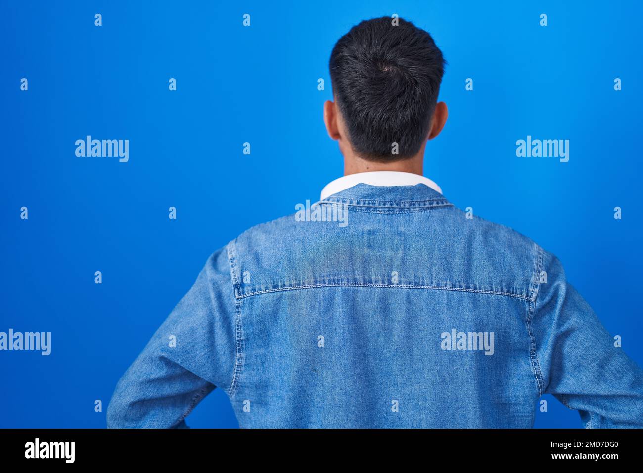 Young hispanic man standing over blue background standing backwards ...