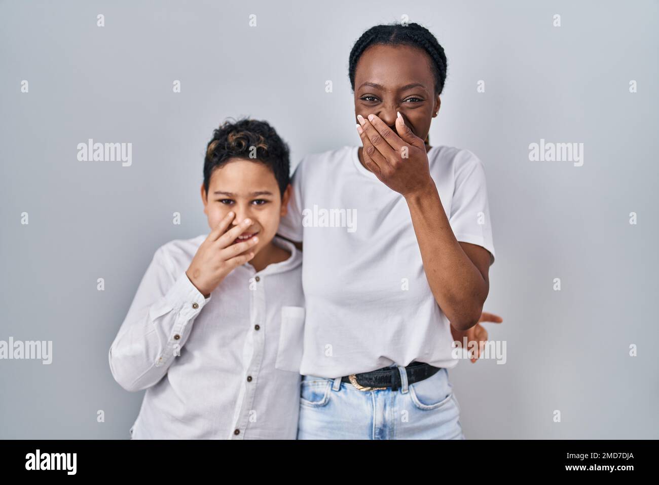 Young mother and son standing together over white background laughing and embarrassed giggle ...