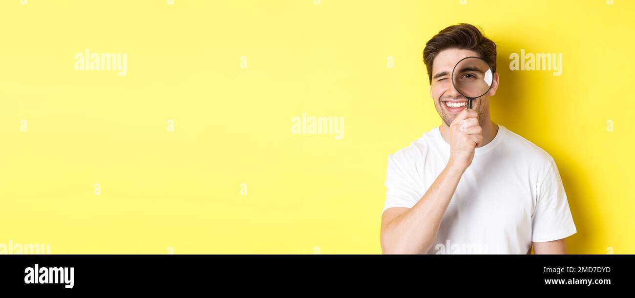 Close-up of young man looking through magnifying glass and smiling ...