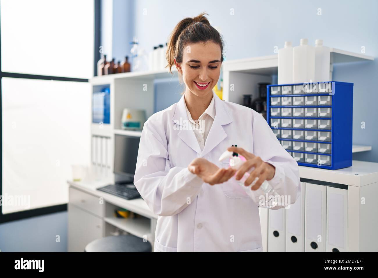 Young woman wearing scientist uniform using sanitizer hands gel at ...