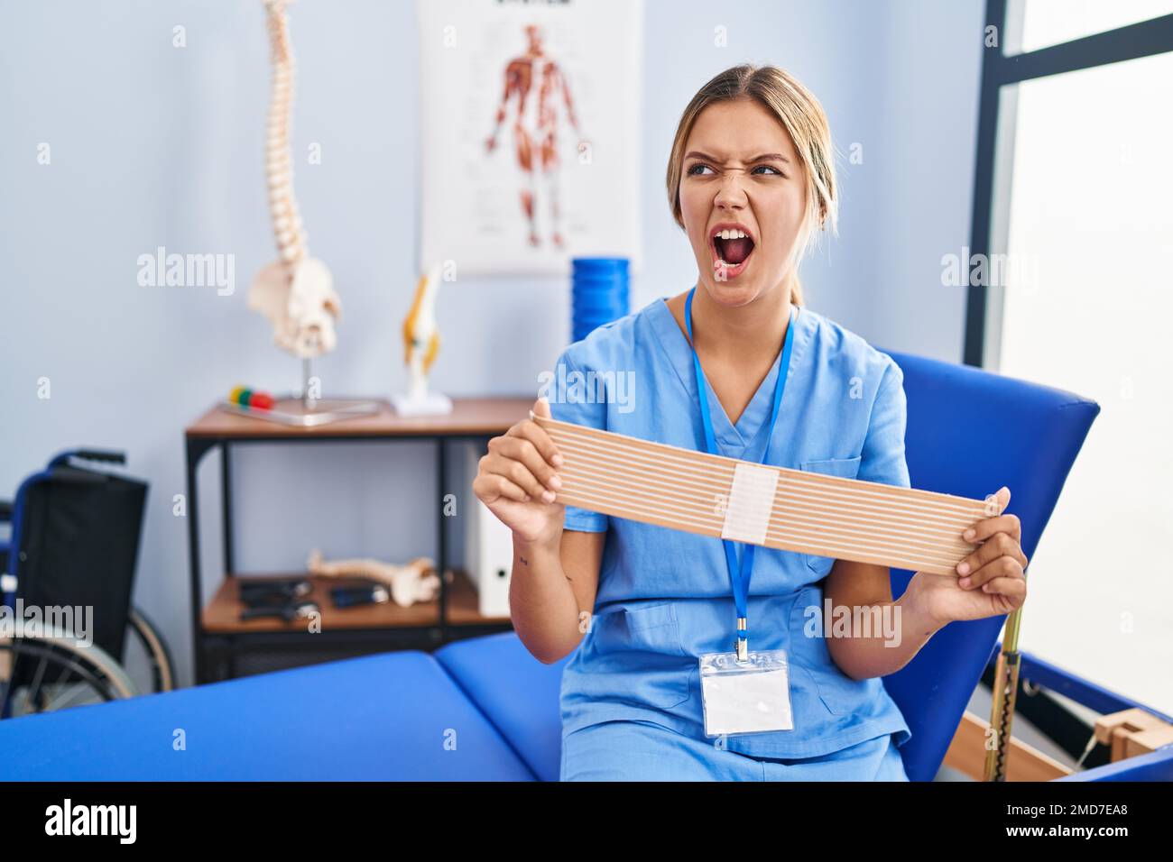 Young blonde woman holding therapy corset angry and mad screaming ...