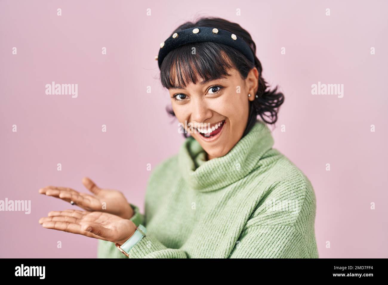 Young beautiful woman standing over pink background pointing aside with ...