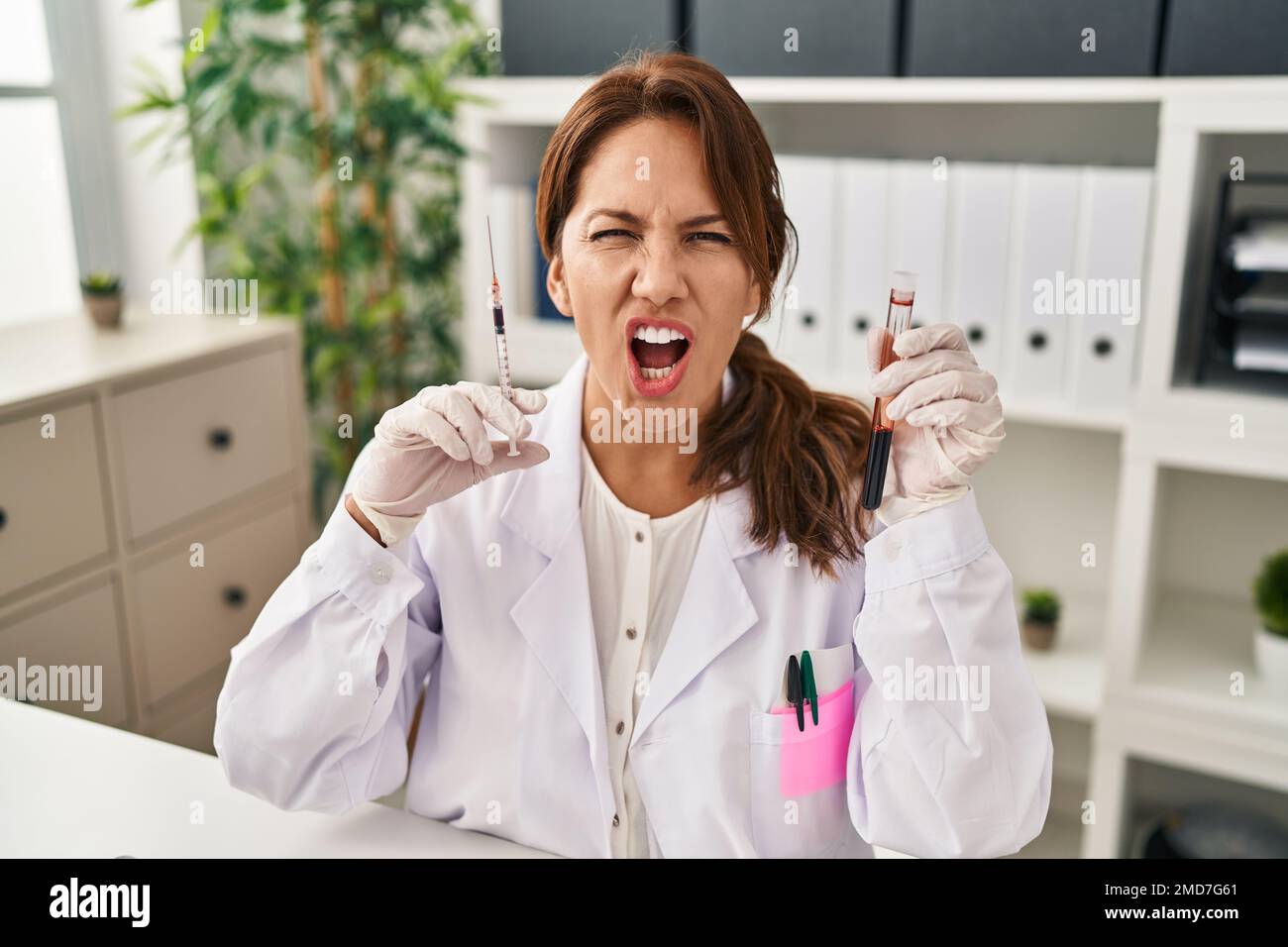 Hispanic doctor woman holding blood sample and syringe angry and mad ...