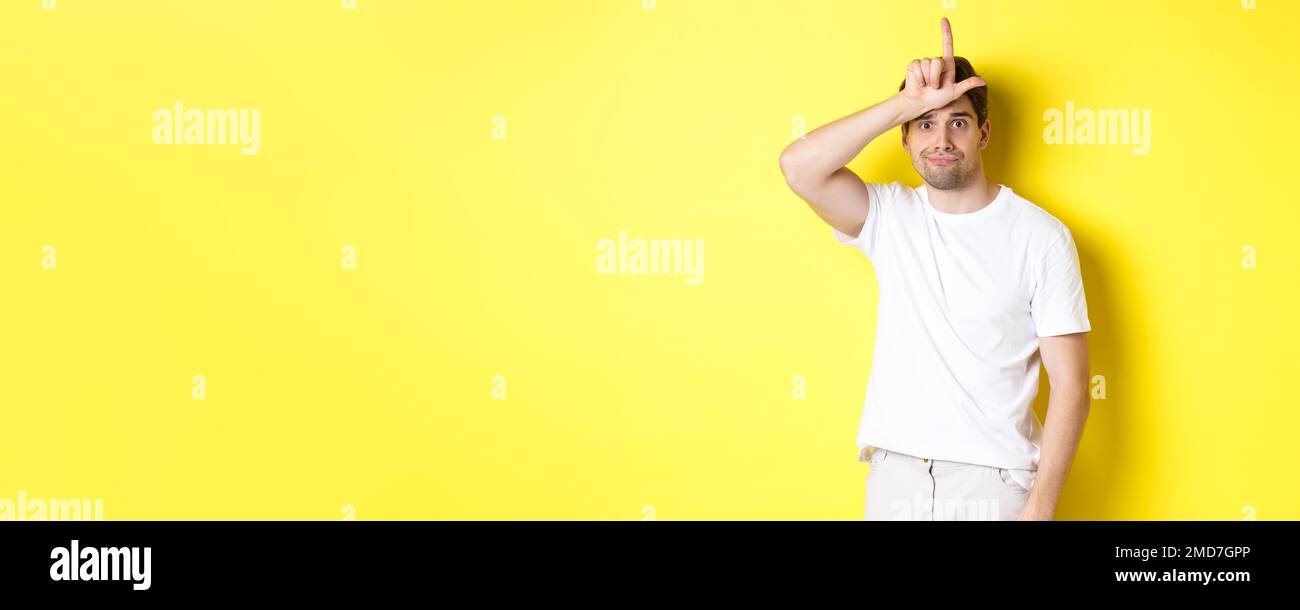 Awkward guy showing loser sign on forehead, looking sad and gloomy ...