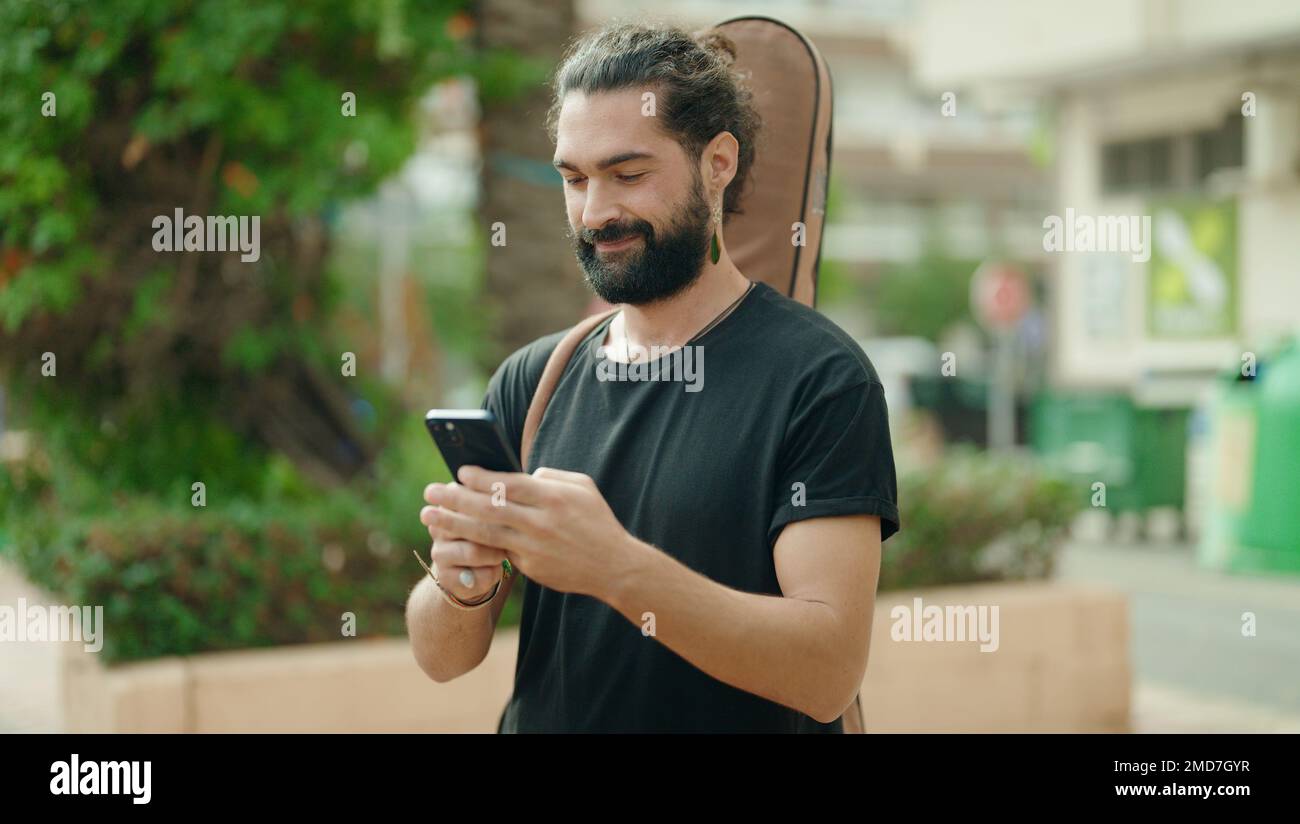 Young hispanic man musician using smartphone holding guitar case at ...