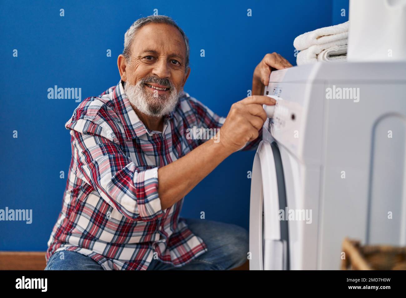Senior grey-haired man smiling confident turning on washing machine at ...