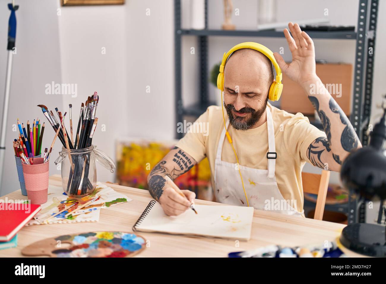 Young bald man artist listening to music drawing on notebook at art ...