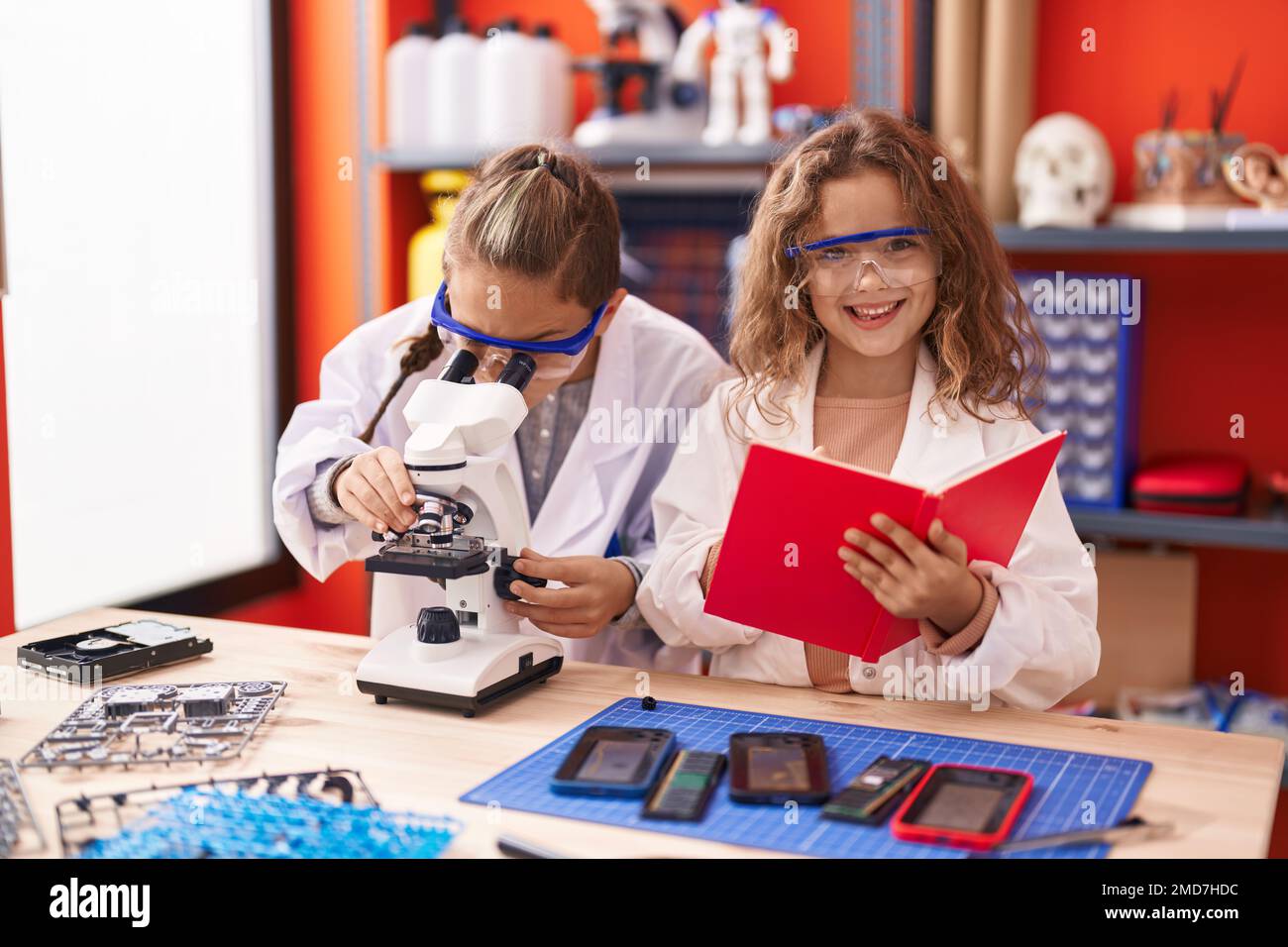 Two kids students using microscope writing on notebook at laboratory ...