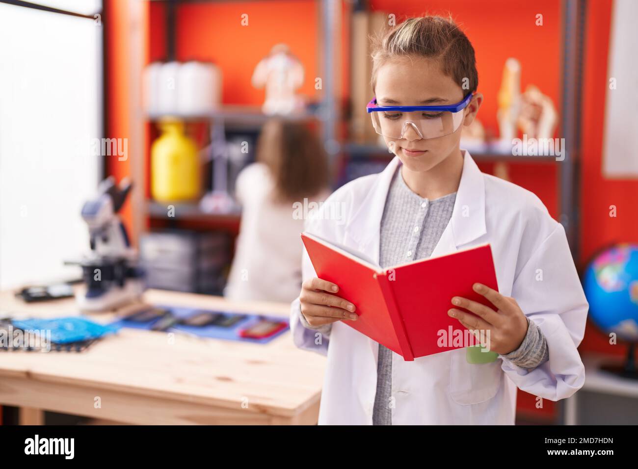 Two kids students using microscope reading notebook at laboratory ...
