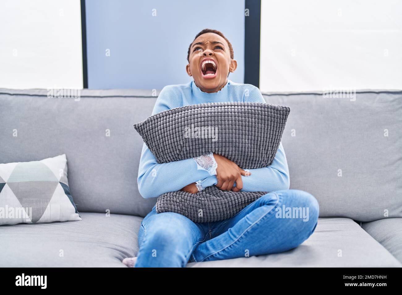 African american woman sitting on the sofa at home hugging pillow angry ...