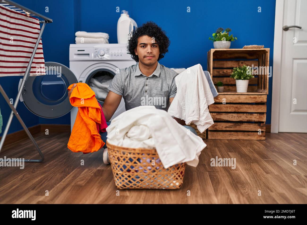 Hispanic man with curly hair doing laundry at laundry room skeptic and ...
