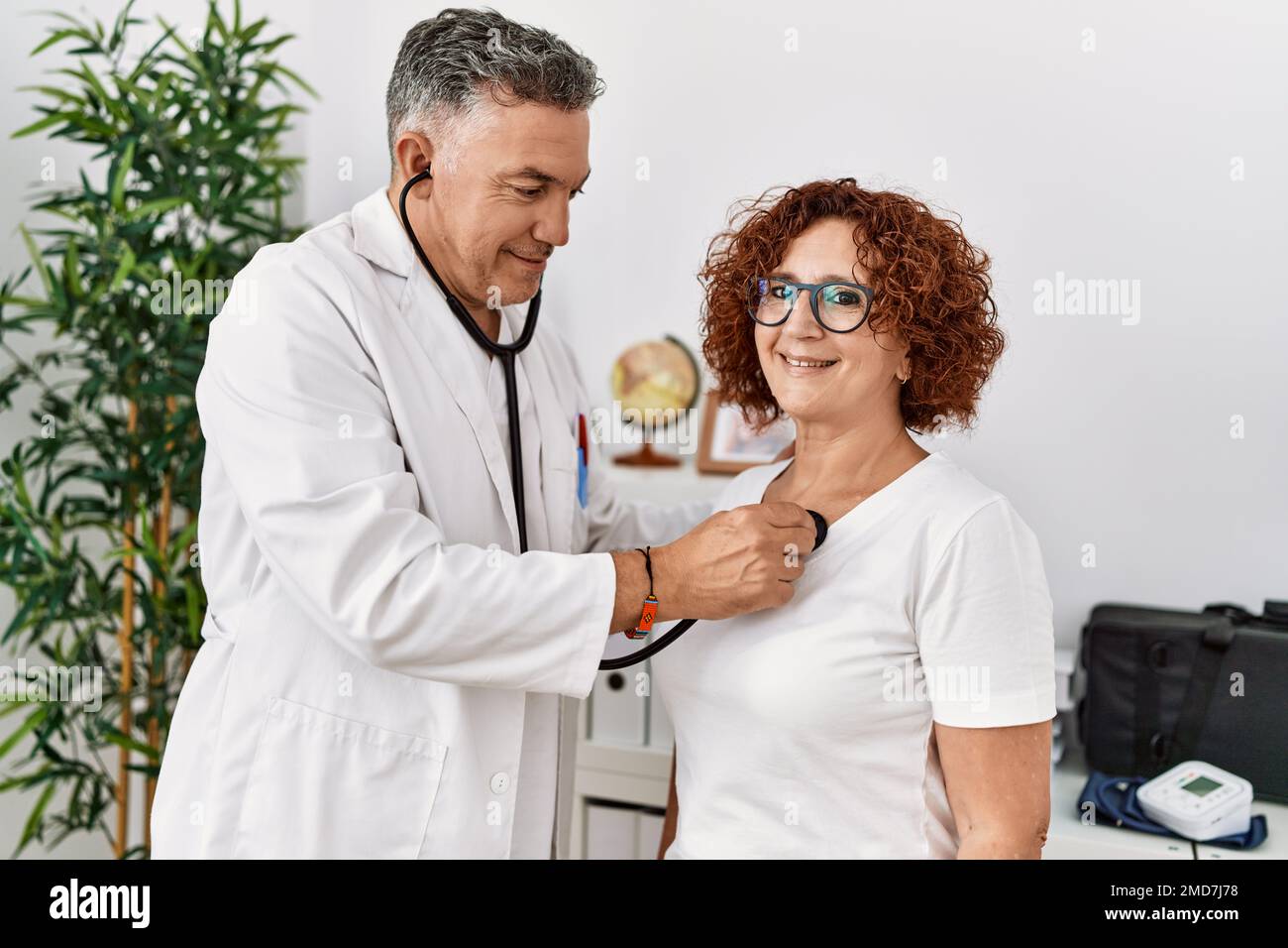Middle age man and woman wearing doctor uniform auscultate heart having ...