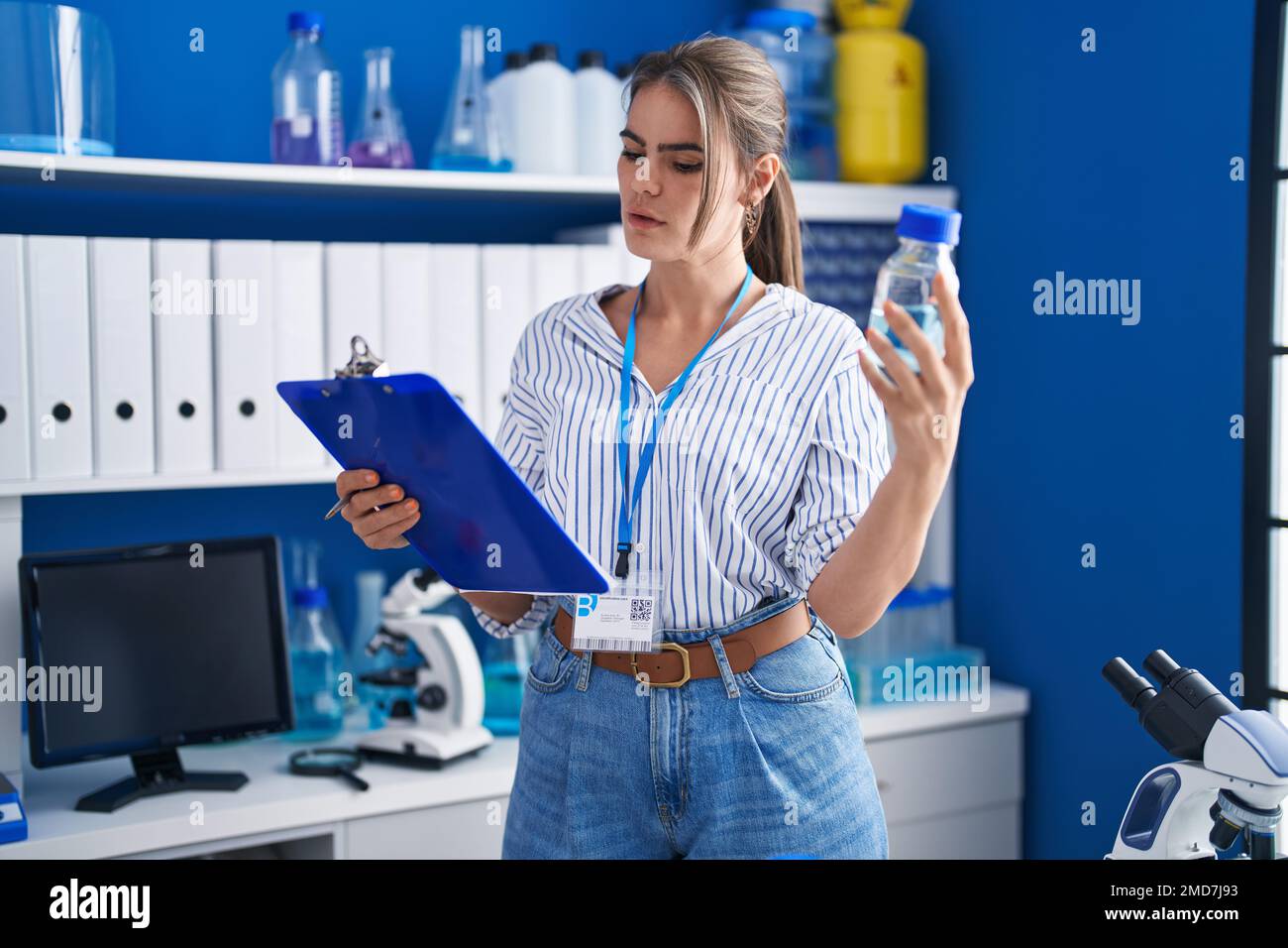 Young woman scientist reading document holding bottle at laboratory ...