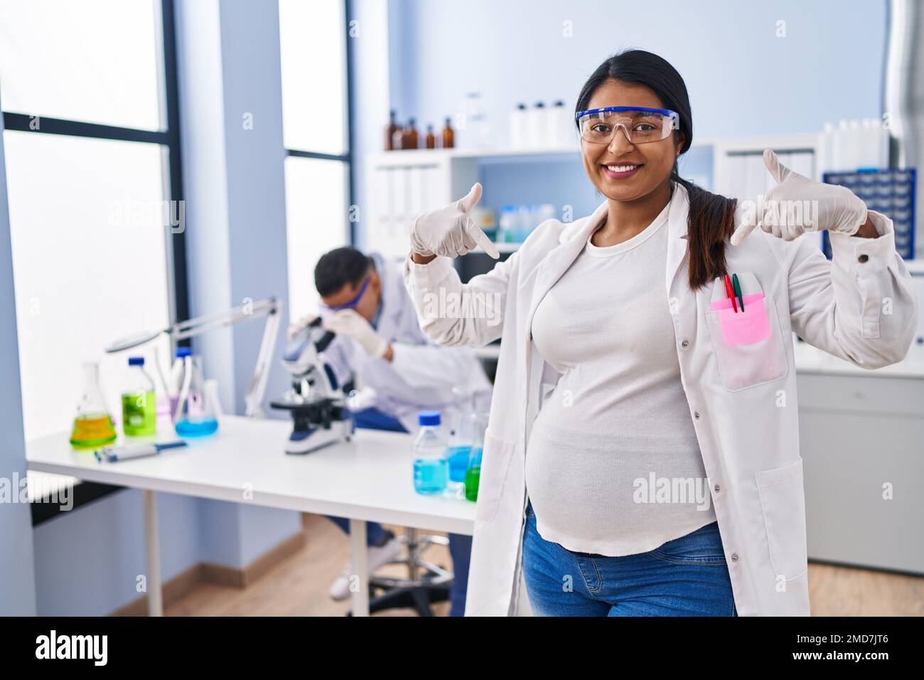 Young hispanic woman expecting a baby working at scientist laboratory looking confident with ...