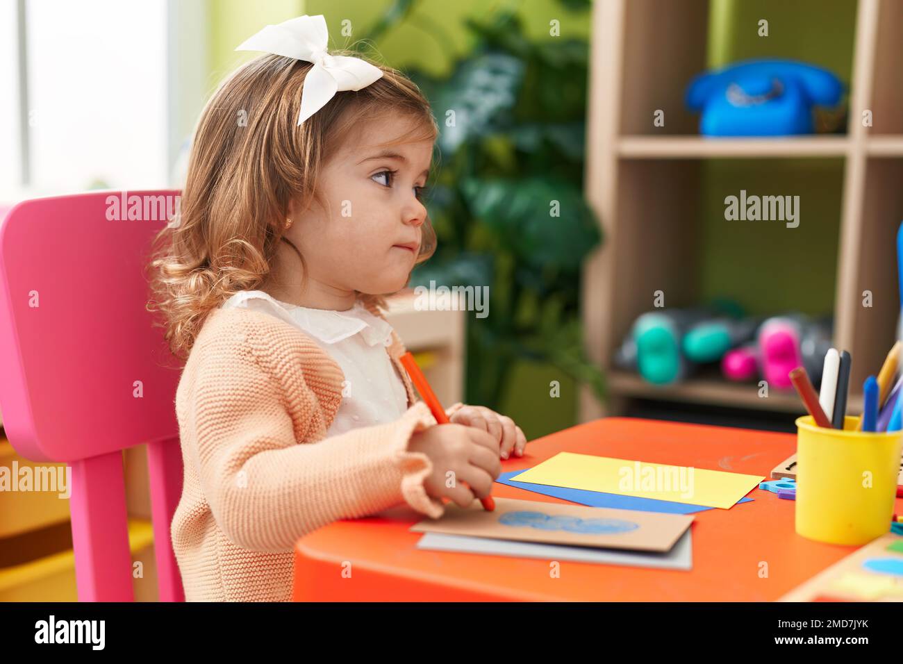 Adorable blonde toddler preschool student sitting on table drawing on paper at kindergarten ...