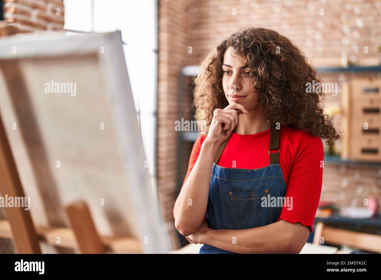 Young hispanic woman artist looking draw with doubt expression at art ...