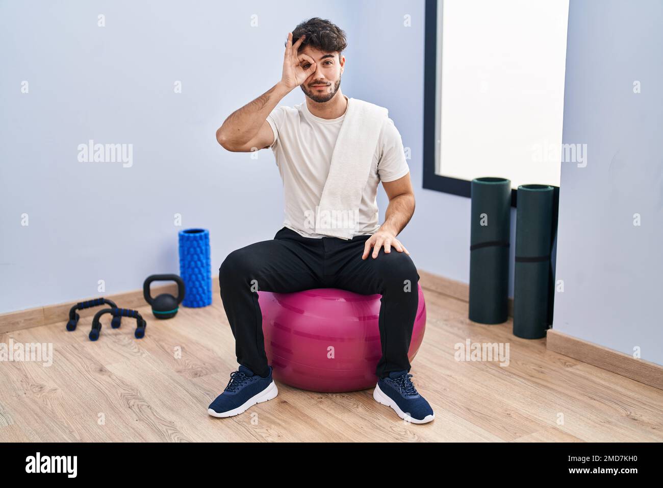 Hispanic man with beard sitting on pilate balls at yoga room doing ok ...