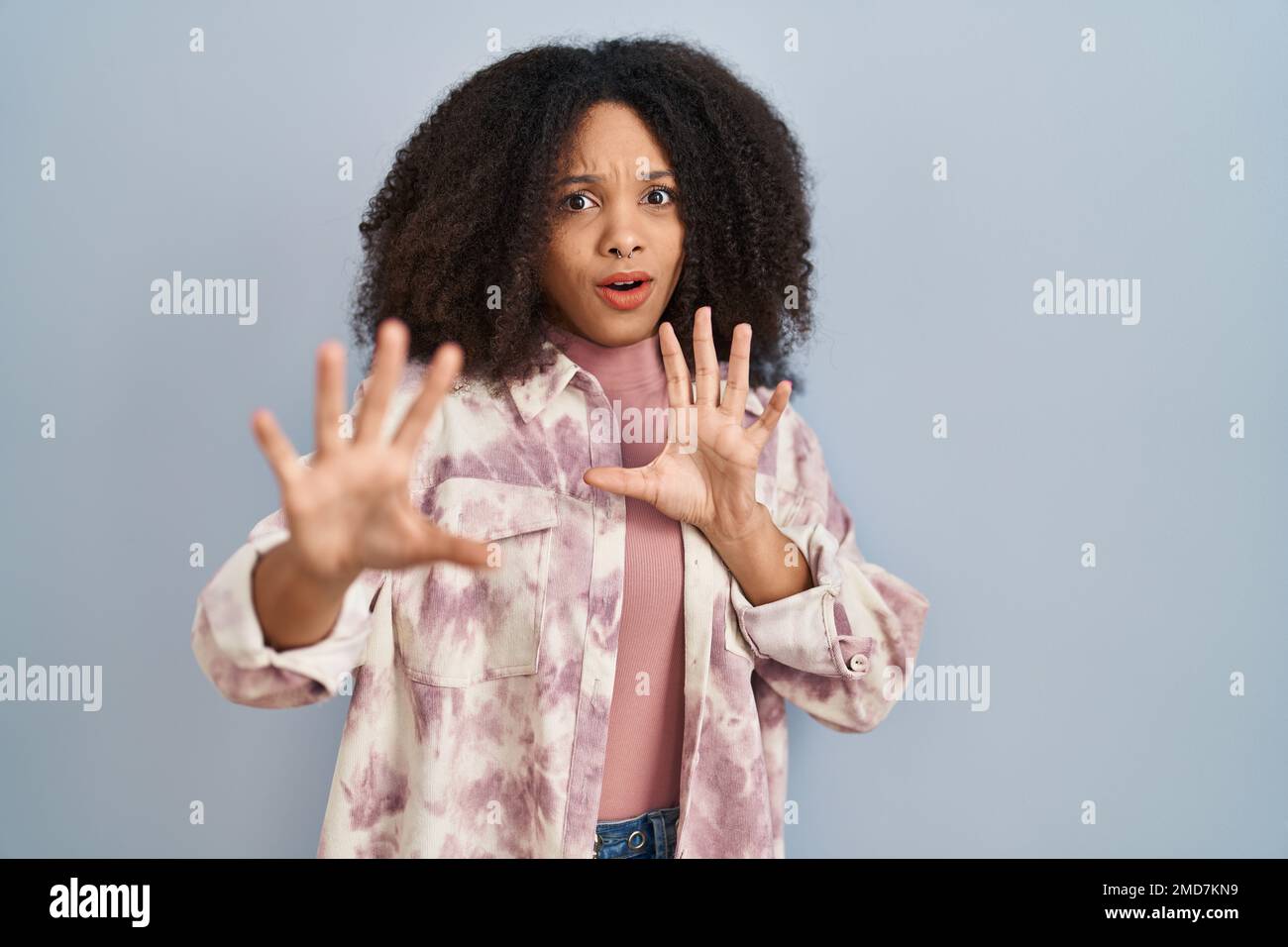 Young african american woman standing over blue background afraid and ...