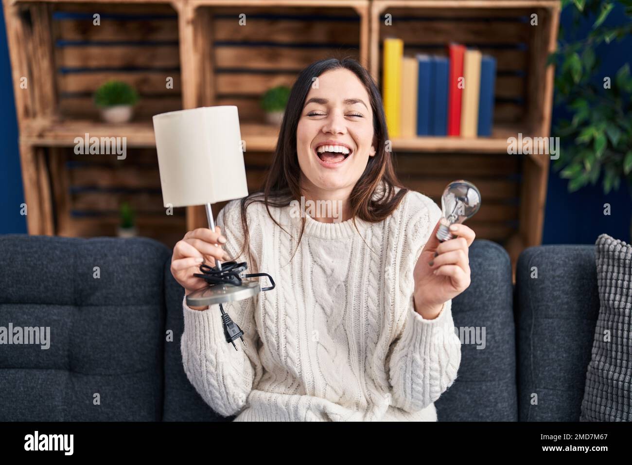 Young brunette woman holding led lightbulb and lamp smiling and ...