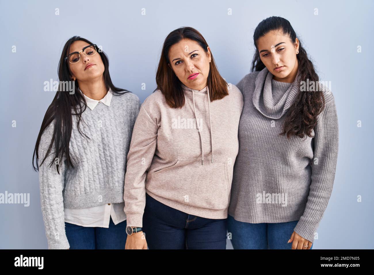 Mother and two daughters standing over blue background looking sleepy ...