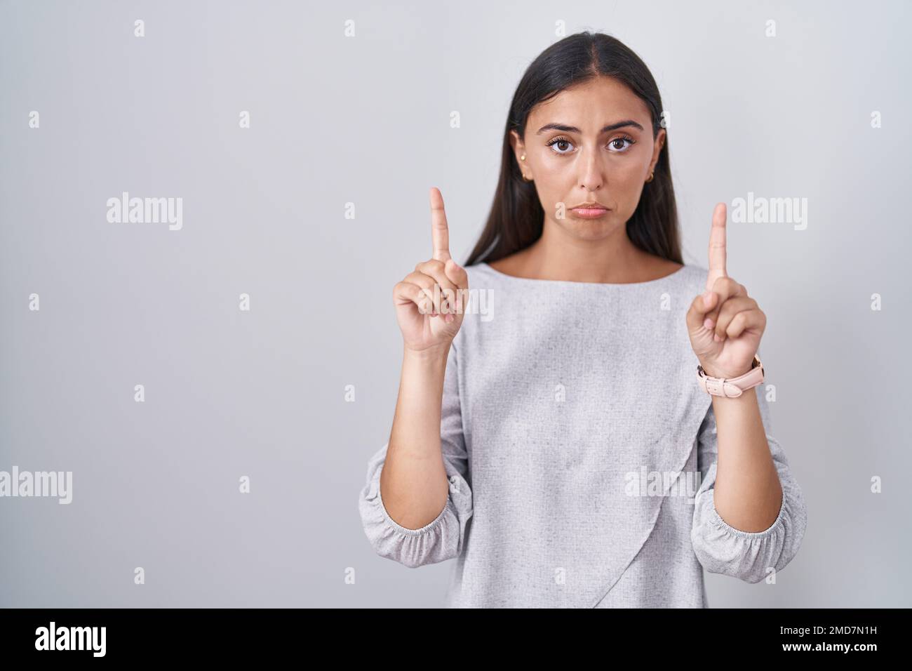 Young hispanic woman standing over white background pointing up looking ...