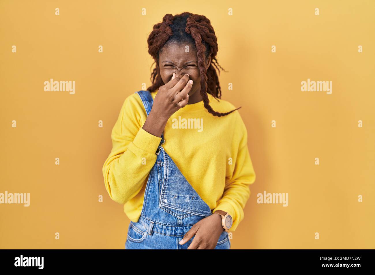 African woman standing over yellow background smelling something stinky ...