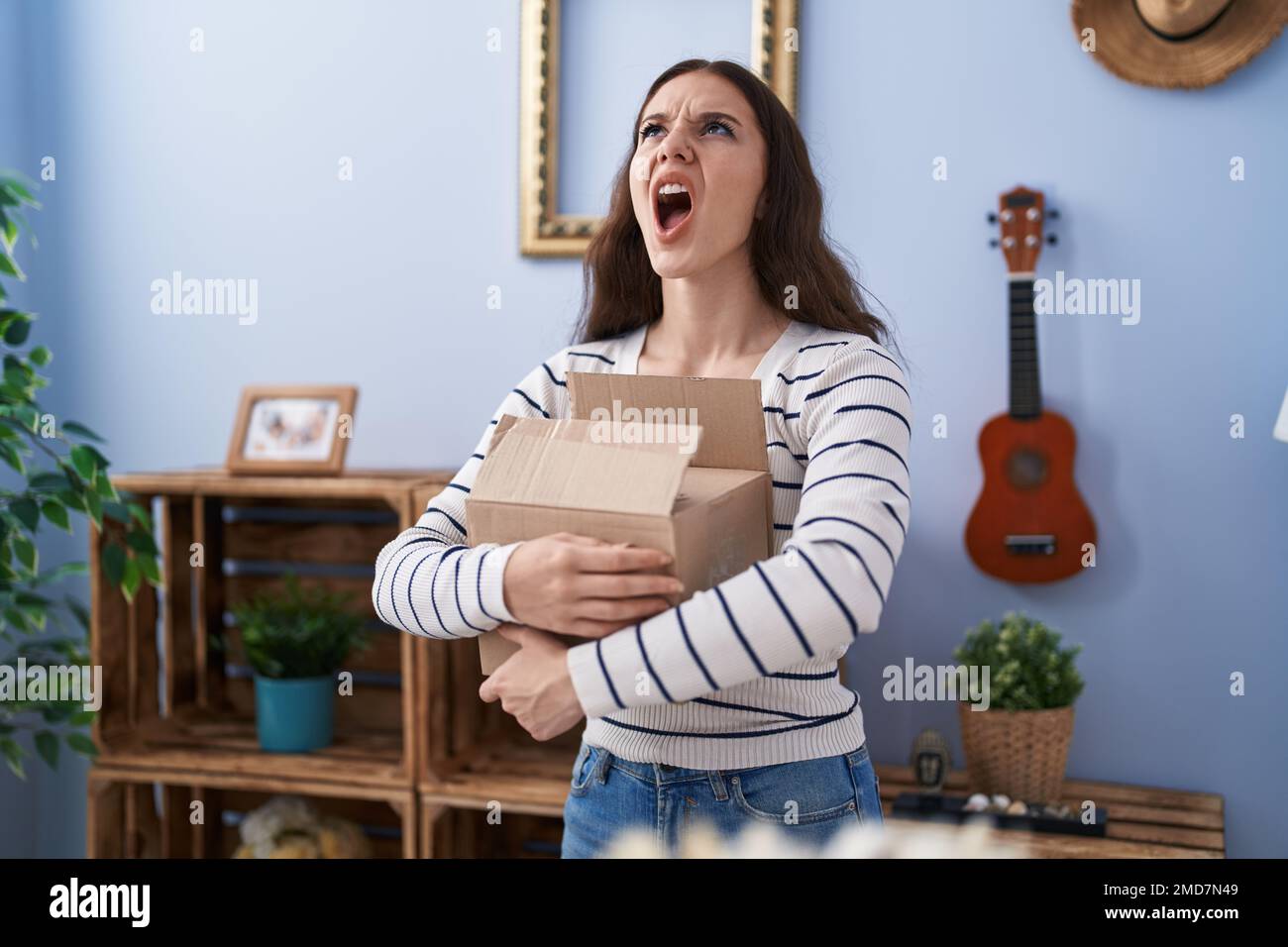 Young hispanic girl opening cardboard box angry and mad screaming ...