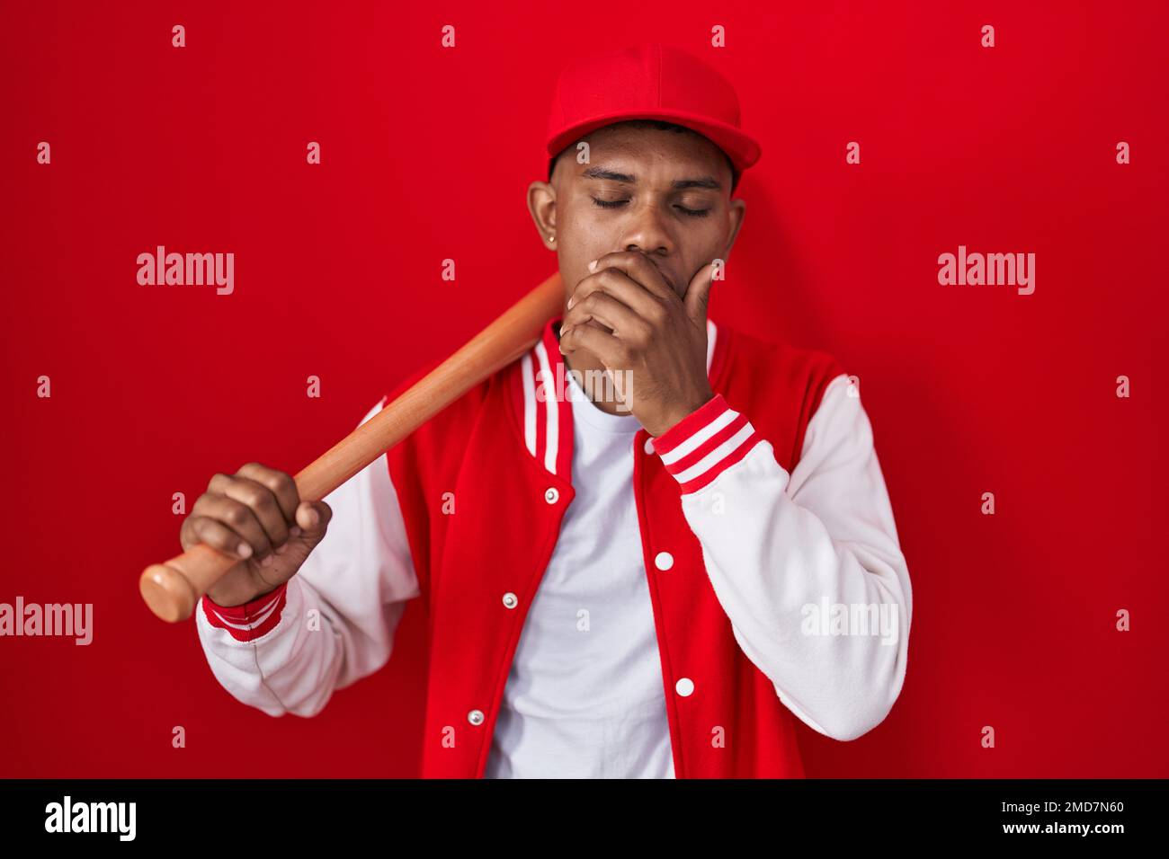 Young hispanic man playing baseball holding bat bored yawning tired ...