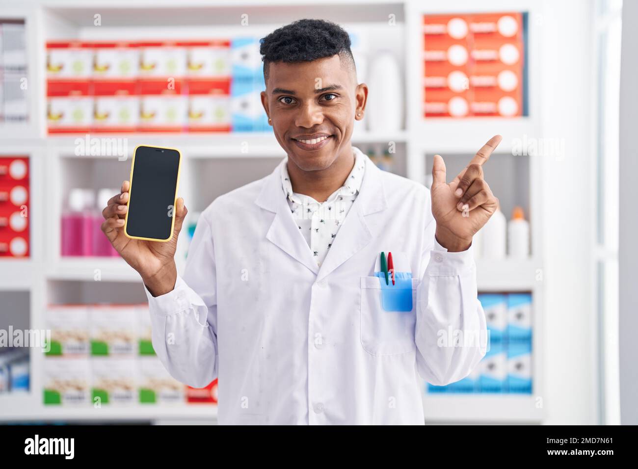 Young hispanic man working at pharmacy drugstore showing smartphone ...