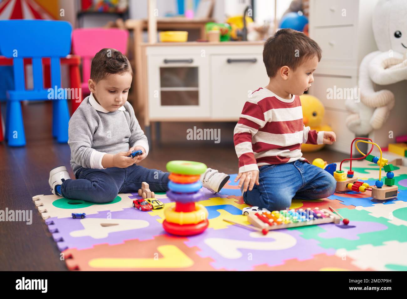 Two kids playing xylophone holding car toy sitting on floor at ...