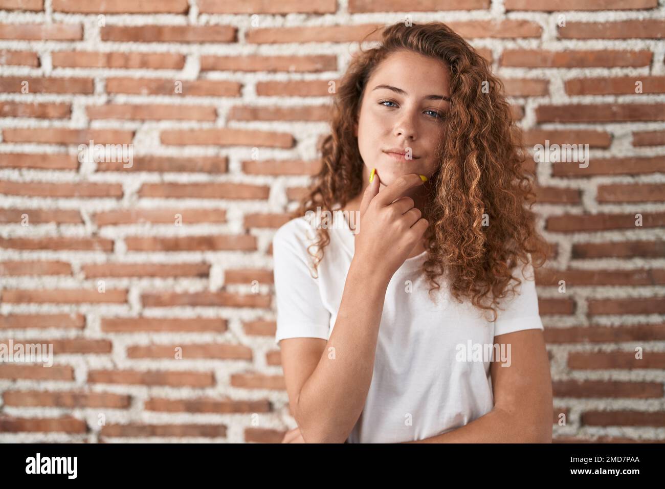 Young caucasian woman standing over bricks wall background looking ...