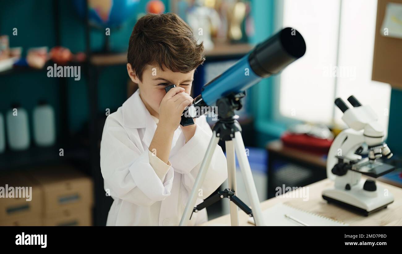 Adorable hispanic boy student using telescope at laboratory classroom ...