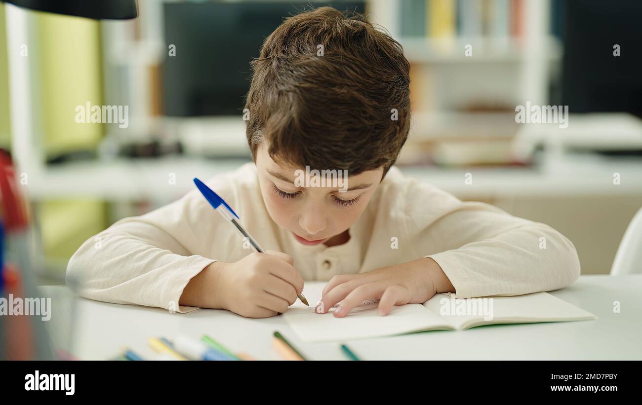 Adorable hispanic boy student writing on notebook at classroom Stock ...