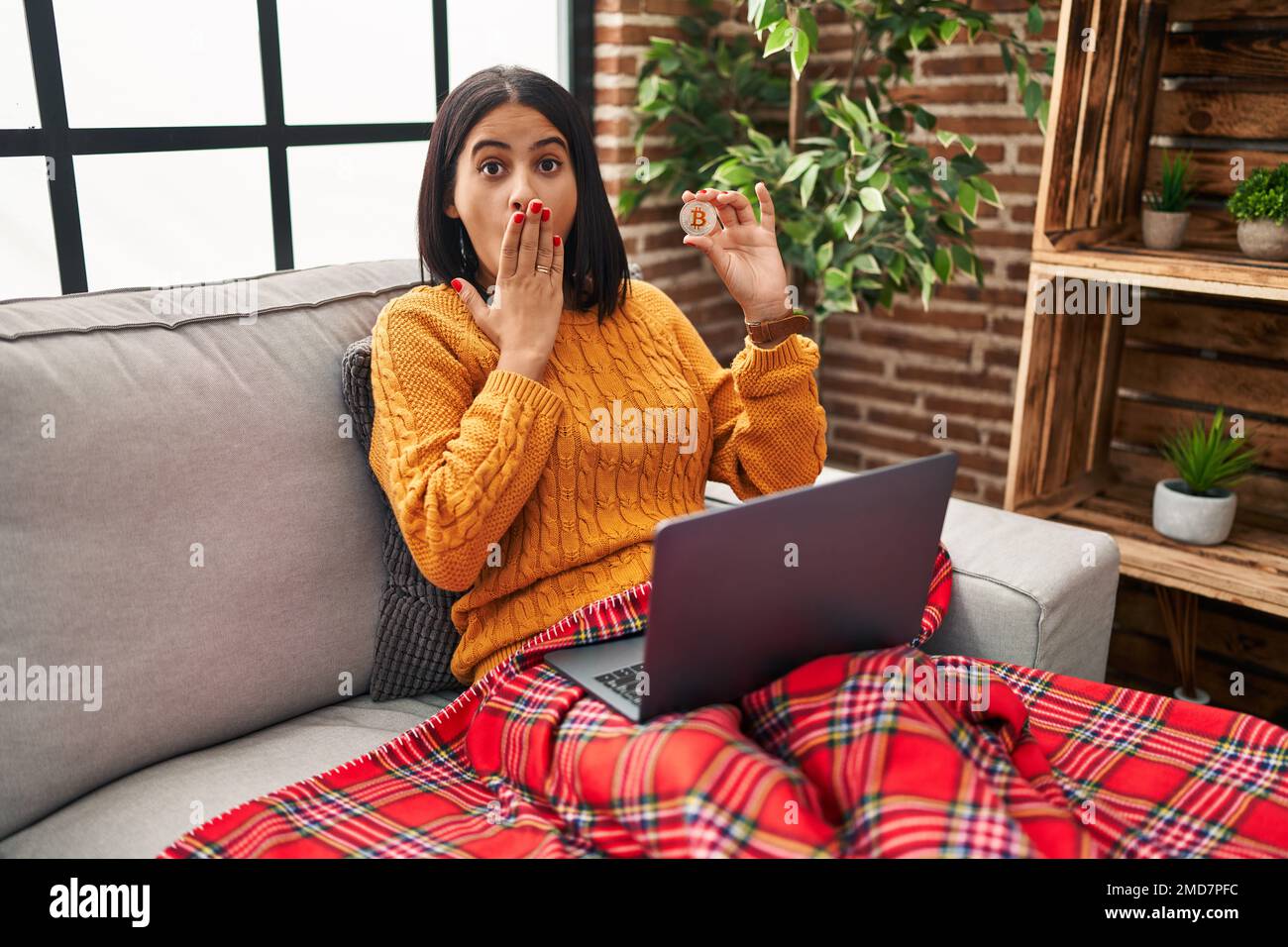 Young hispanic woman using laptop holding virtual currency bitcoin ...