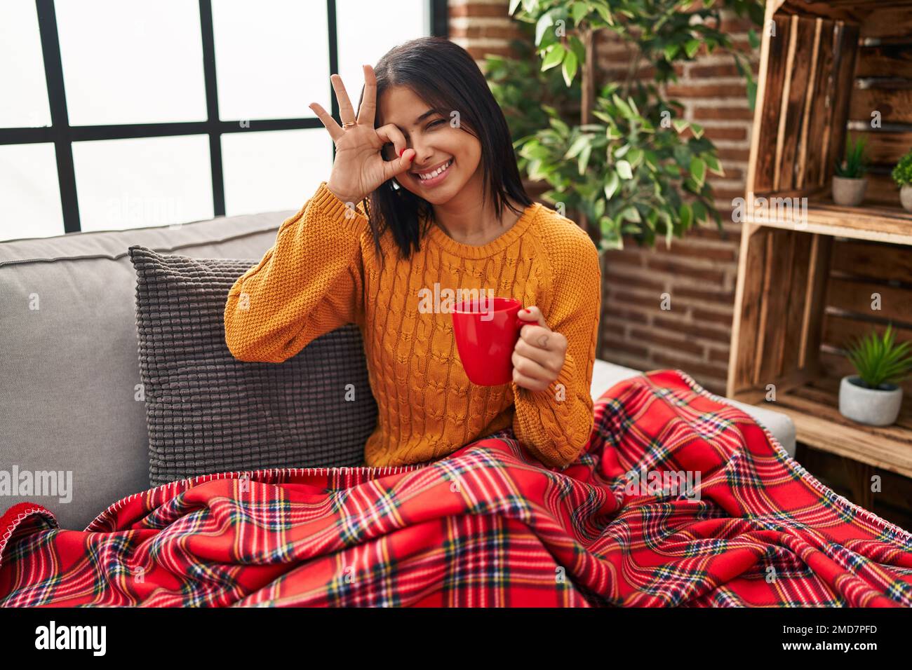 Young hispanic woman sitting on the sofa drinking a coffee at home ...