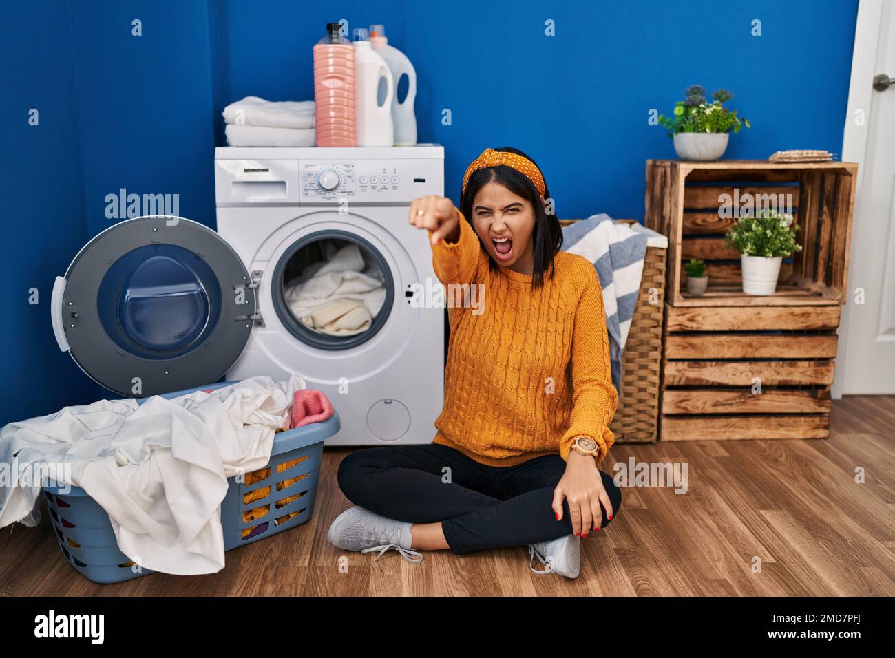 Young hispanic woman doing laundry pointing displeased and frustrated ...