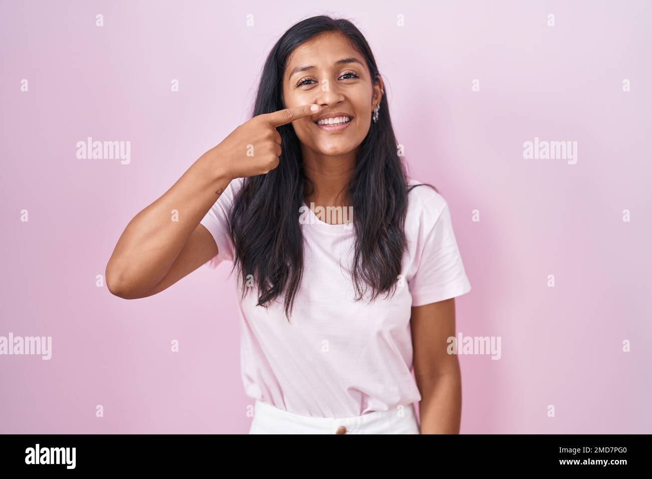 Young hispanic woman standing over pink background pointing with hand ...