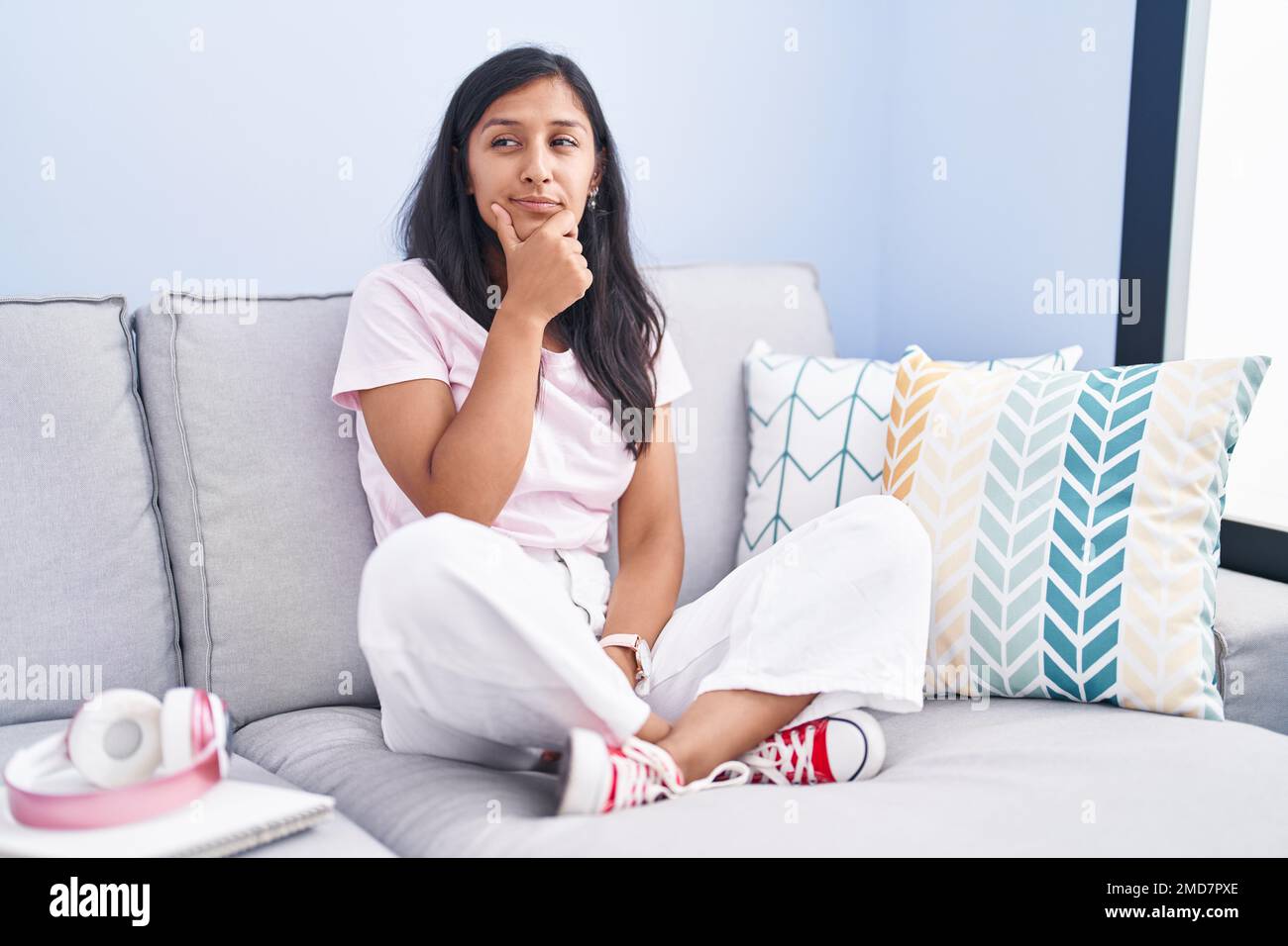 Young hispanic woman sitting on the sofa at home looking confident at ...