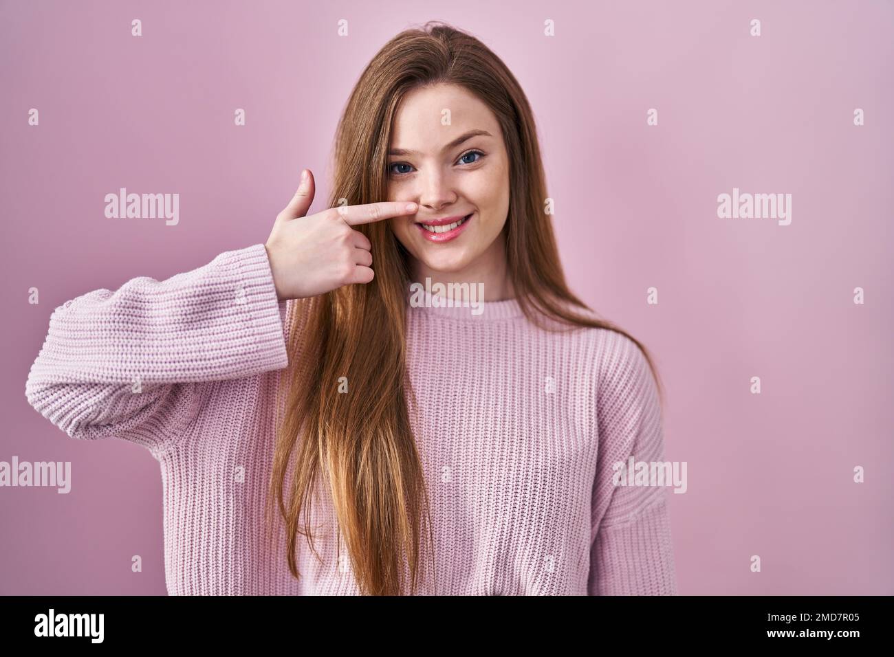 Young caucasian woman standing over pink background pointing with hand ...